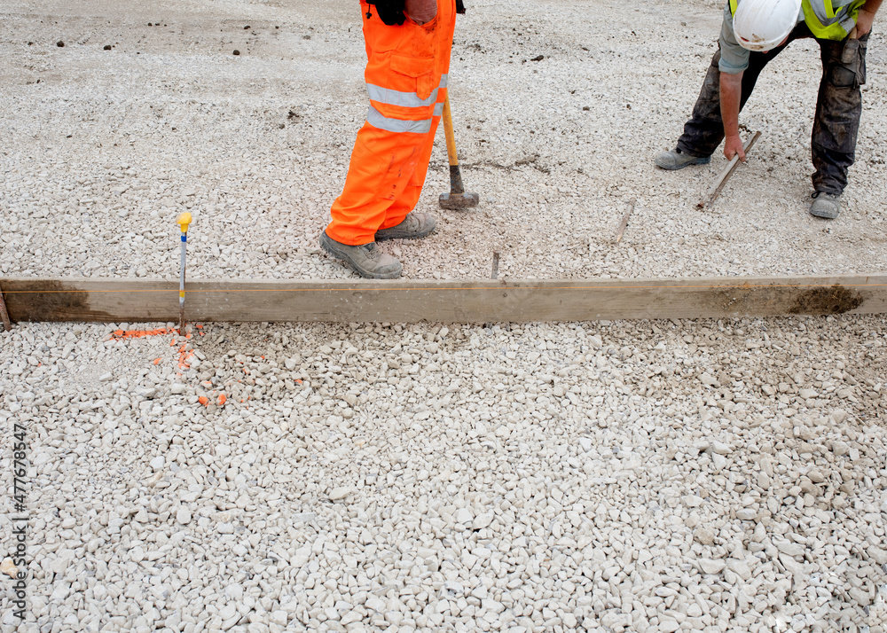 Groundworker in orange safety hi vis trousers fixing a timber along ...