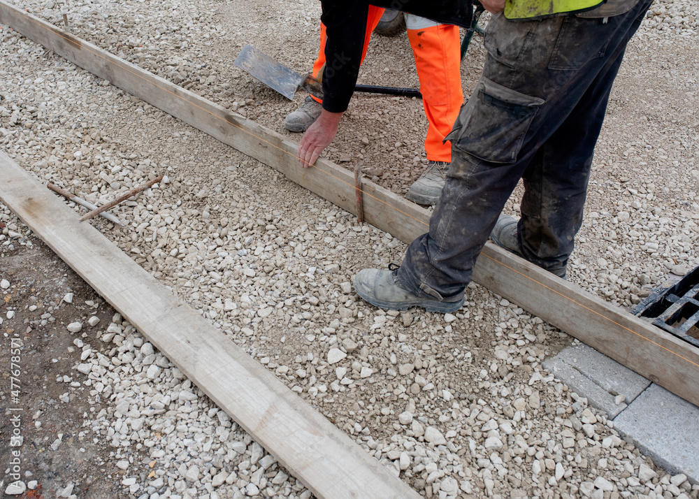 Groundworker in orange safety hi vis trousers fixing a timber along ...