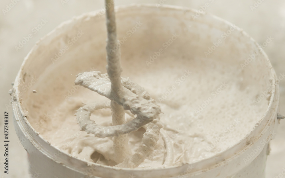 the process of mixing plaster mortar putty mixer in a bucket close-up ...