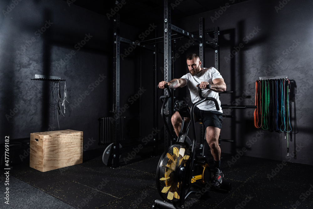 Strong active athlete muscular fit man with big muscles riding air bike ...