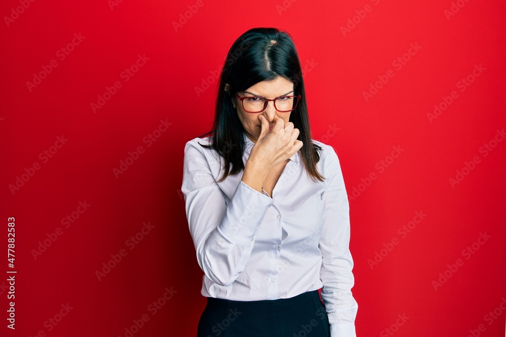 Young hispanic woman wearing business shirt and glasses smelling ...