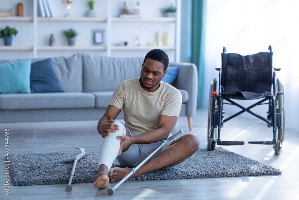 Black man with injured leg sitting on floor after falling down, having ...