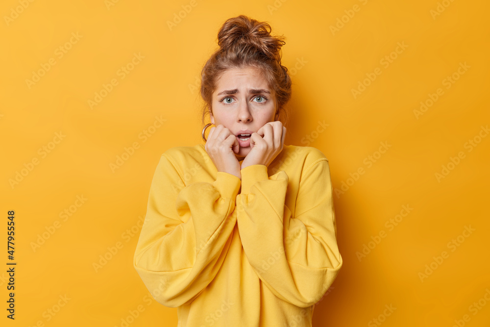 Concerned anxious European woman trembles from fright grabs face stands ...