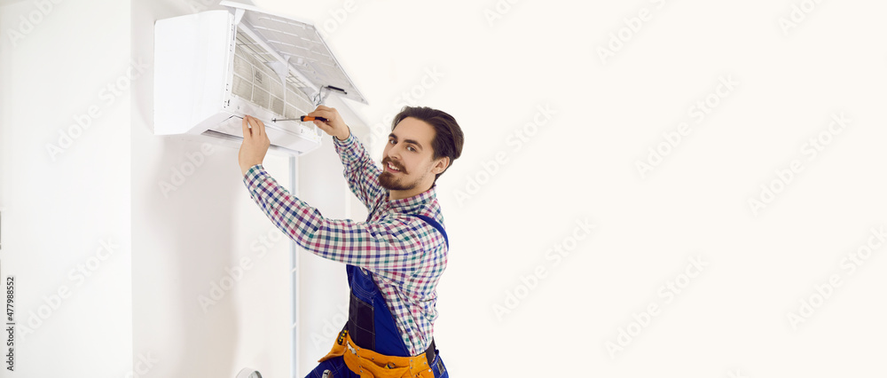 Happy technician opens up modern wall mounted air conditioner to check ...