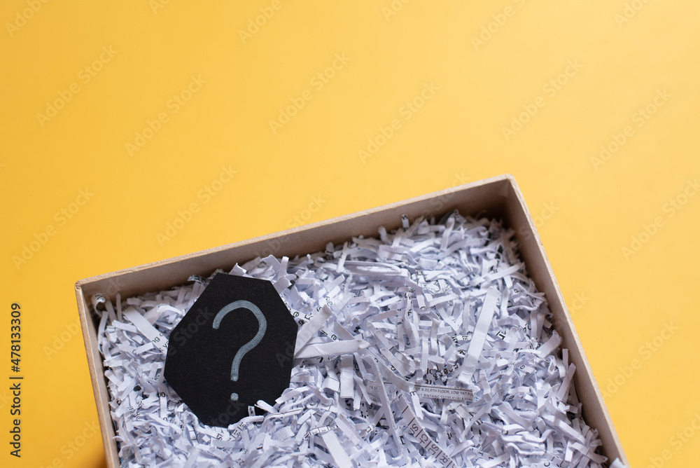 Question mark and shredded paper in abox against yellow background ...