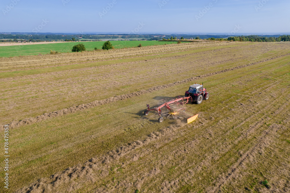Aerial view on a tractor that collects hay in rows with a disc rake ...
