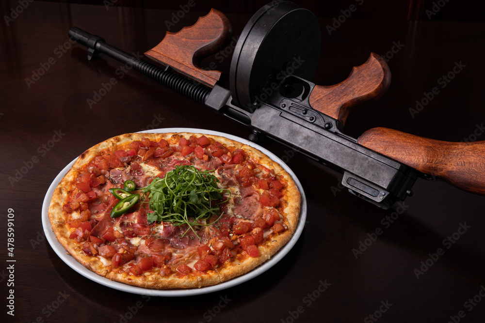 Thompson submachine gun on a dark brown table and a ham pizza with ...
