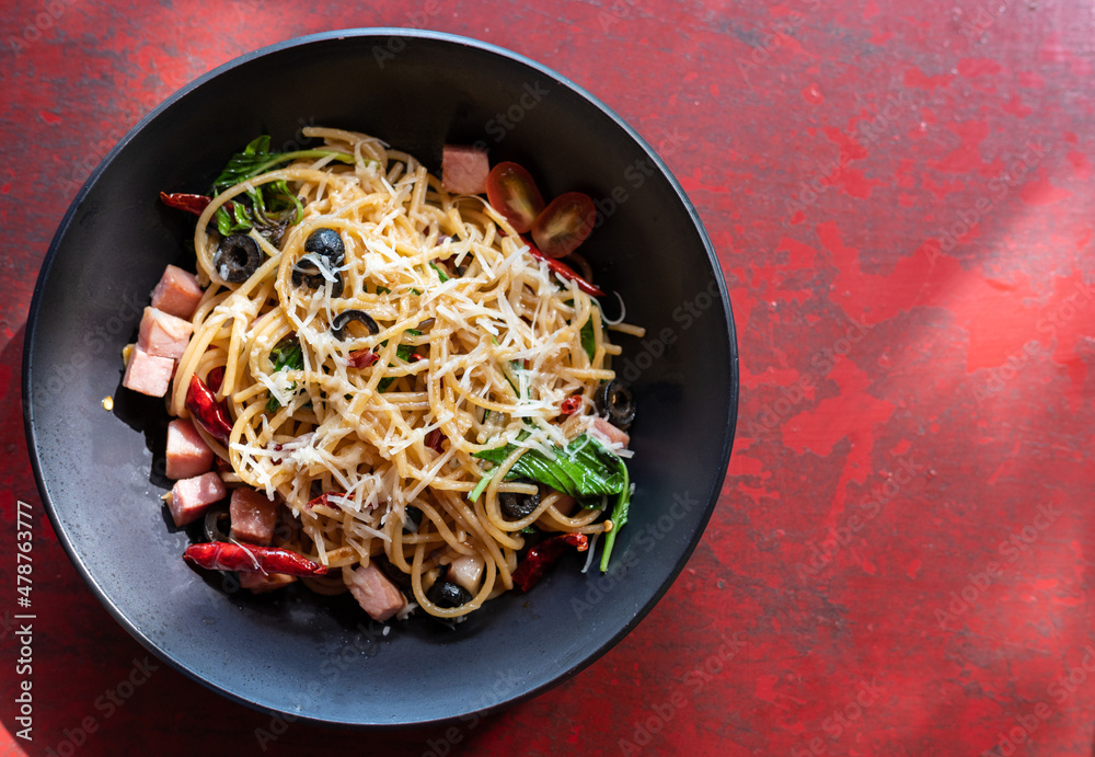 Spaghetti with chili paste and ham served on red table. Spaghetti is ...