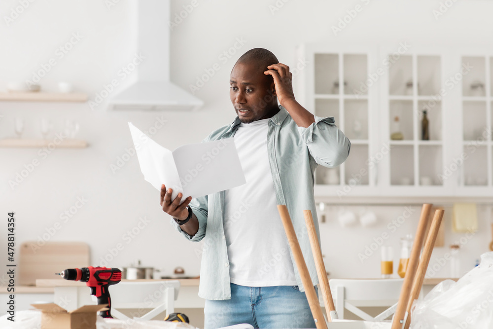 Confused black man having hard time assembling furniture and reading ... Confused black man having hard time assembling furniture and reading ...