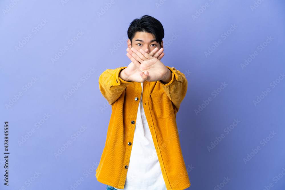 Young Chinese man isolated on purple background making stop gesture ...