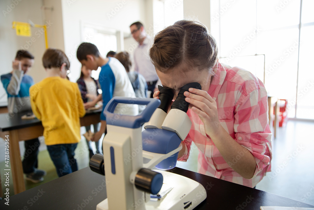 Schoolgirl taking notes at microscope science laboratory classroom ...