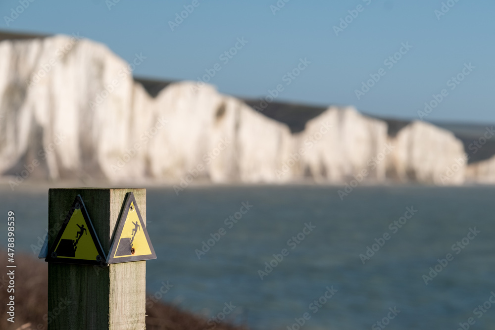 Yellow and black danger sign warning of erosion at the cliff edge. In ...