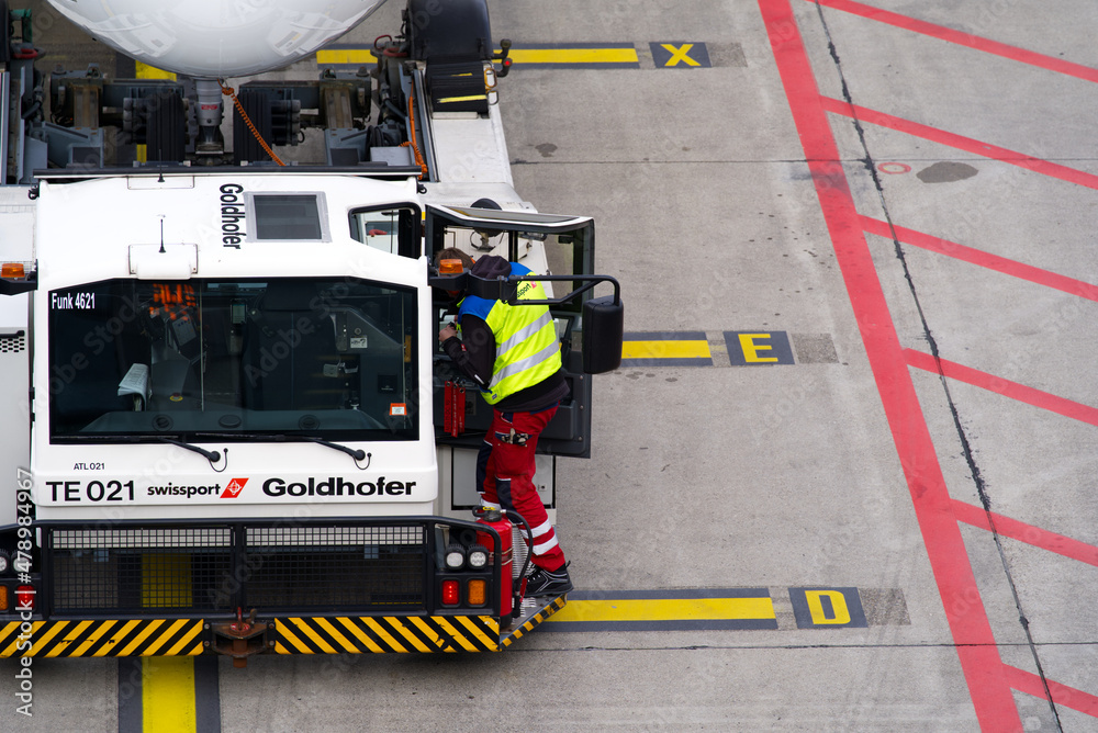 Driver getting on aircraft tug at Zürich Airport on a cloudy winter day ...