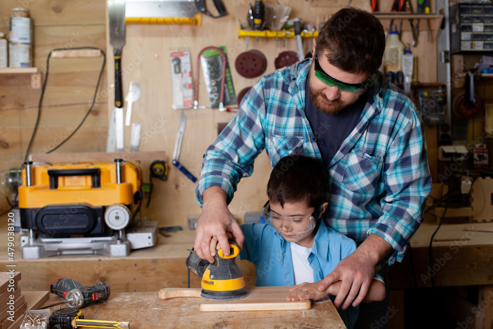 Father carpenter and son boy work in the workshop. Master dad teaches ...