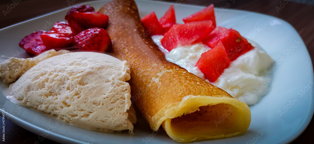 Crêpe mit Erdbeeren Melone Vanilleeis und Sahne angerichtet auf einem ...