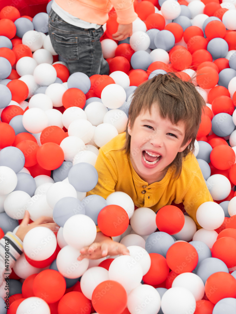 Laughing boy plays in ball pit. White and red plastic balls in dry ...