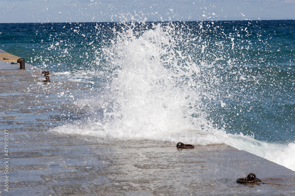 Waves crash against a stone harbor wall with bollards and the seawater ...