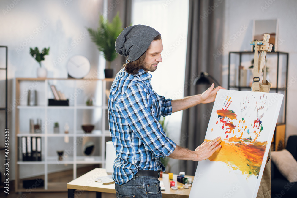 Skilful male artist drawing with colorful paintings on easel at home ...