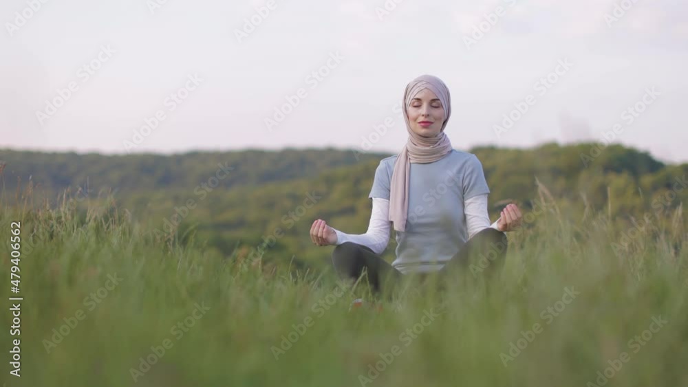 Peaceful young lady in hijab meditating with closed eyes in the park ...