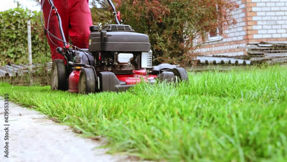 Garden red lawnmower. Low angle of side view of worker mowing lawn ...