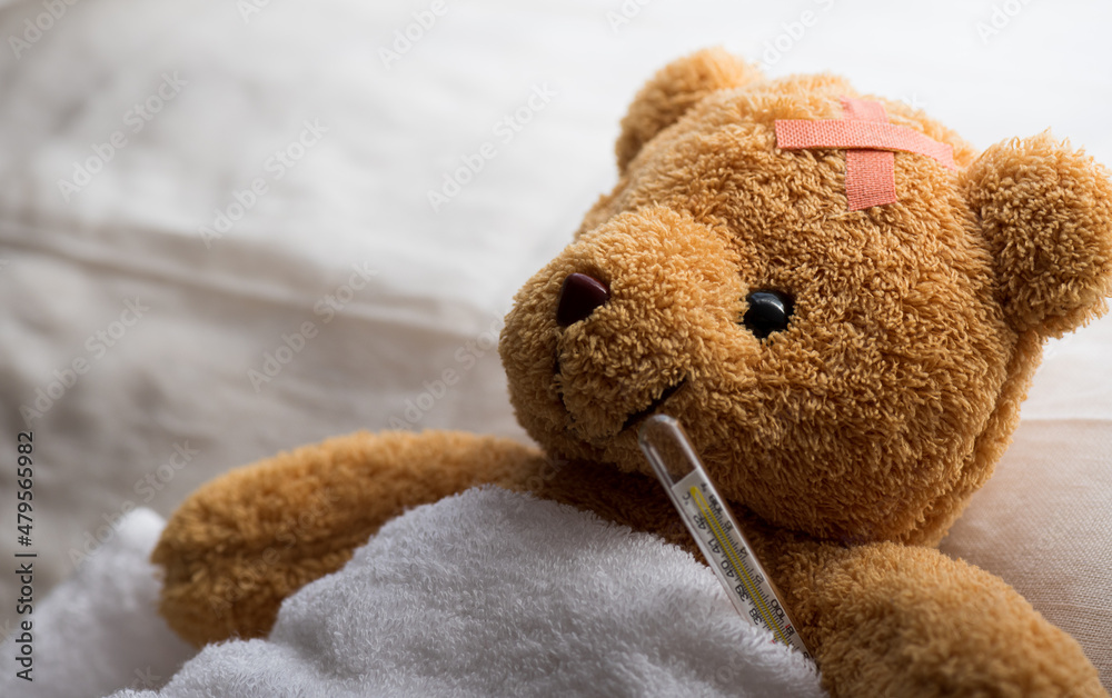 Teddy bear lying sick in hospital bed with with thermometer and plaster ...