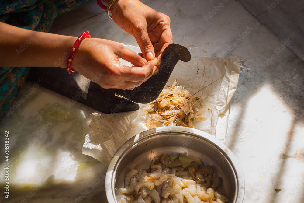 bengali indian woman cutting or dressing raw shrimp for cooking in desi ...