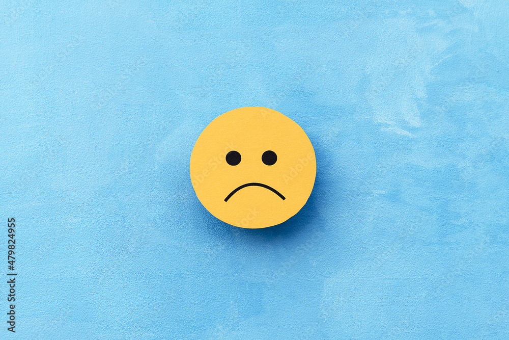 Yellow sad smiley face on a blue background. The concept of negative ...