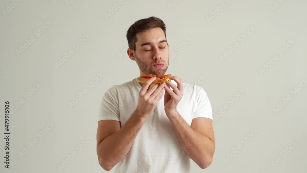 Studio portrait of hungry young man biting into slice of pizza ...