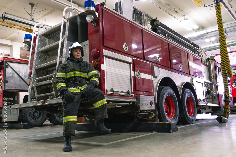 A firefighter in special clothes is sitting on the running board of a ...