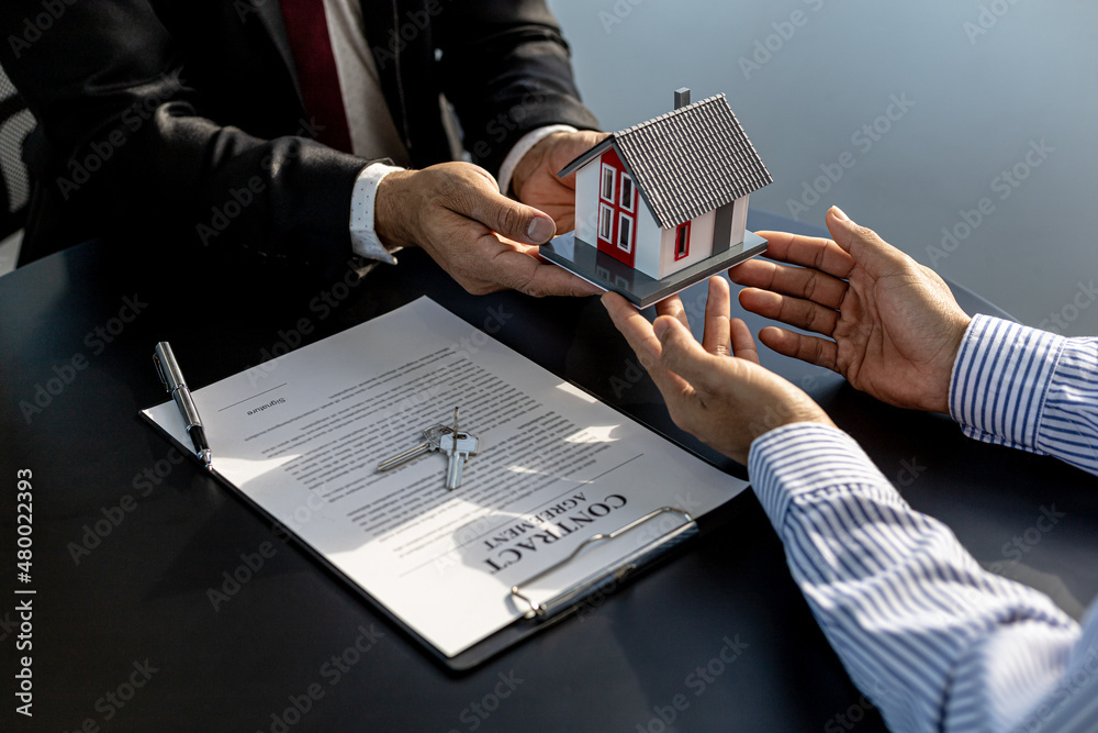 Two people holding a small model house, the home salesman handing over ...