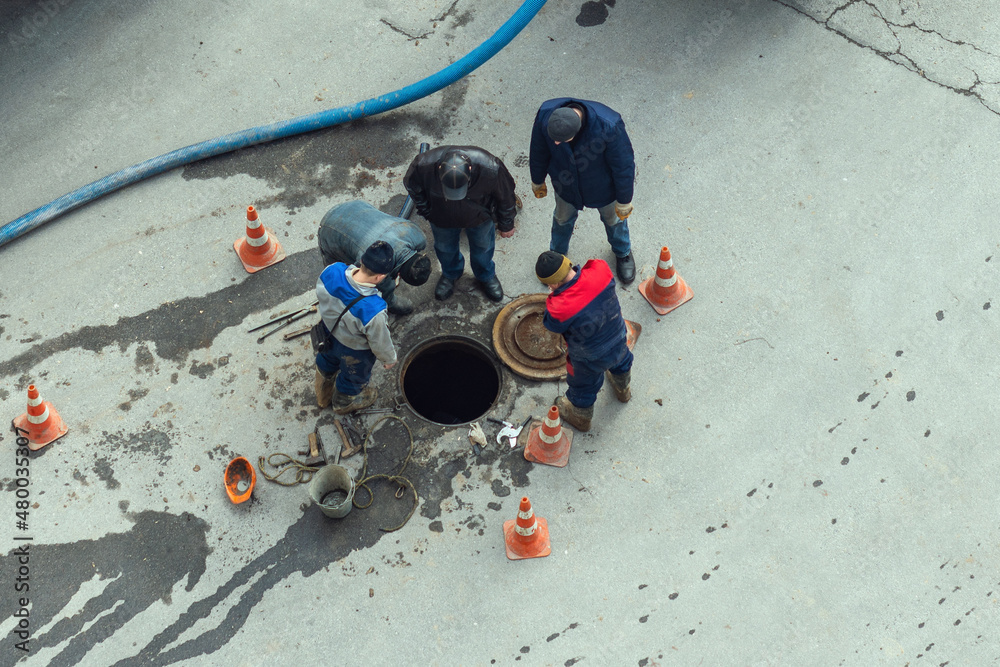 Foto de Workers stand over an open manhole on the street. Repair of ...
