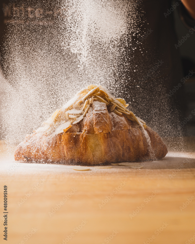 Chefs hands with small sieve over baking Croissants in a bakery shop ...