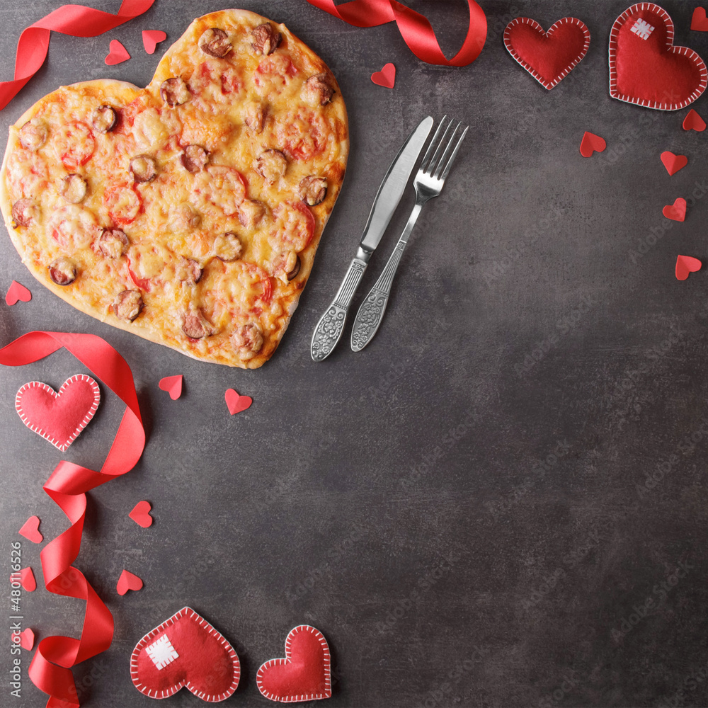 Romantic dinner. Heart shaped pepperoni pizza and bright red ribbon on ...