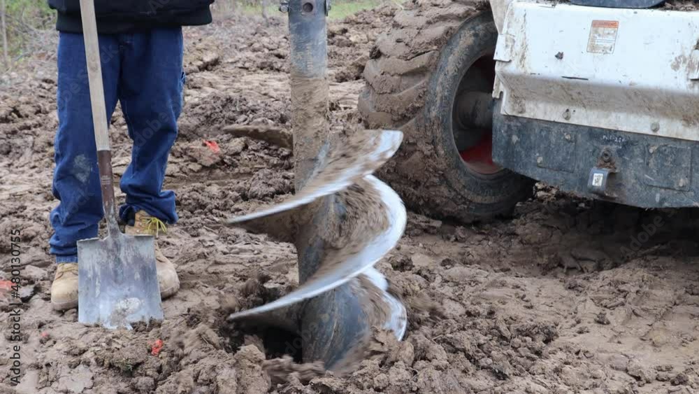 Close up of hydraulic auger mounted on skid steer loader digging a post ...