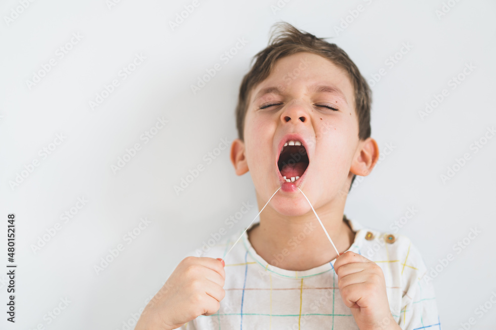 Cute boy pulling loose tooth using a dental floss. The boy's first milk ...