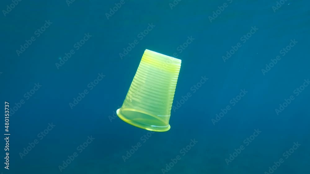Plastic pollution, yellow plastic cup slowly drifting underwater in the ...