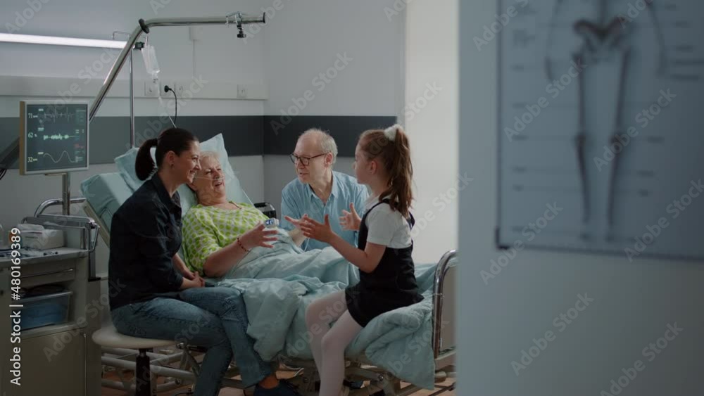 Young girl visiting aged woman in hospital ward bed with mother and old ...