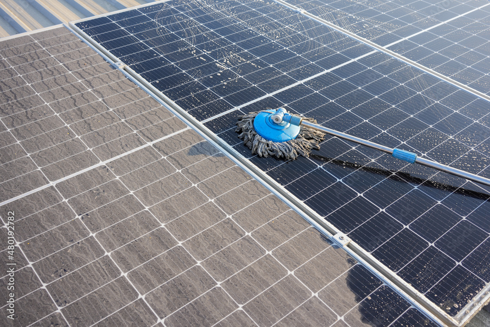 Man using a mop and water to clean the solar panels that are dirty with ...