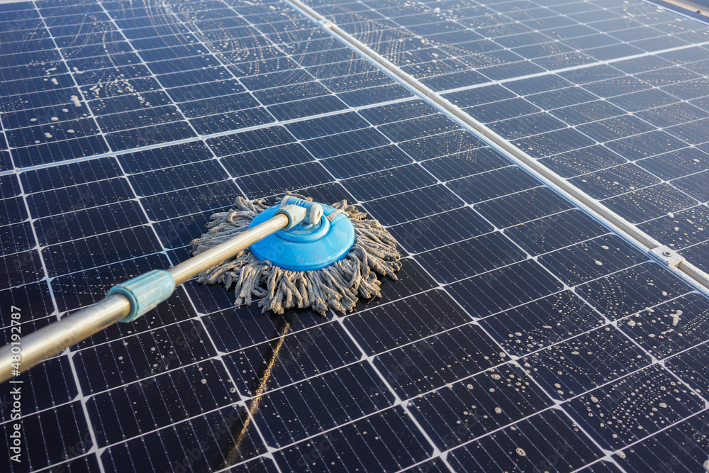 Man using a mop and water to clean the solar panels that are dirty with ...