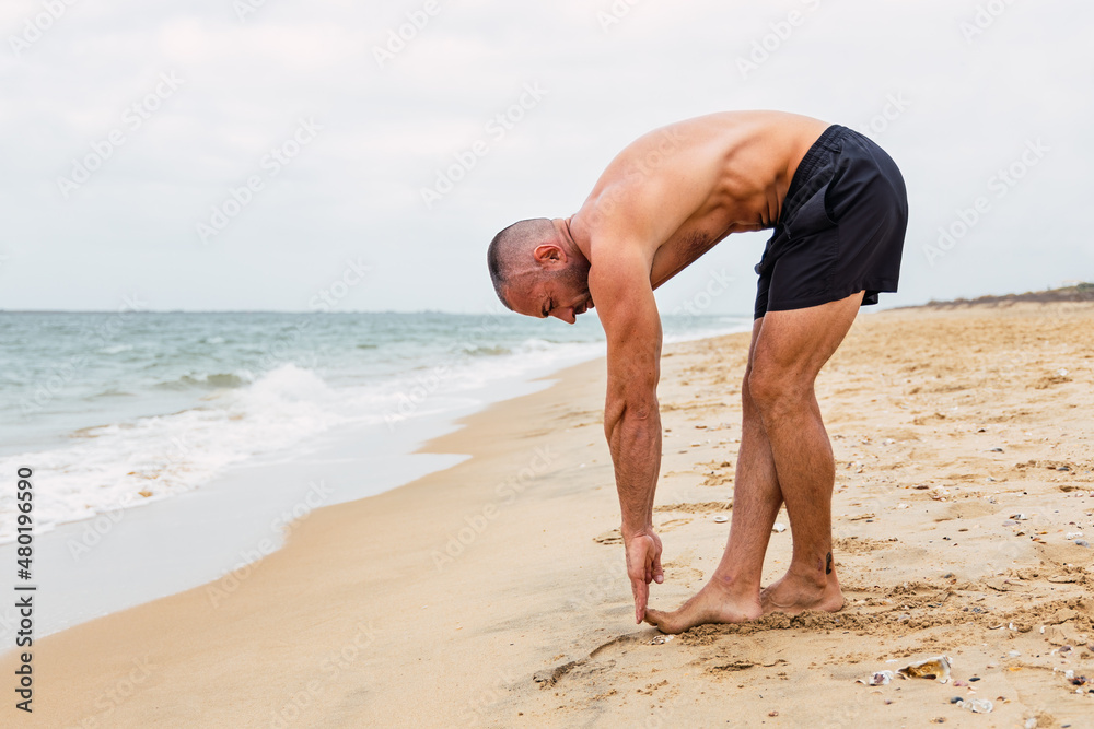 Shirtless man stretching and bending forward on beach Stock Photo ...