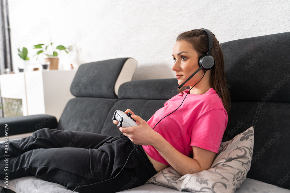 A young female gamer playing a console game lying on a couch at home in ...