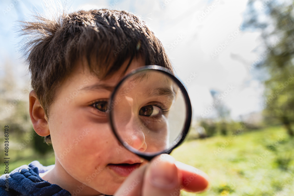 Happy, curious child exploring with a magnifying glass with focus on ...