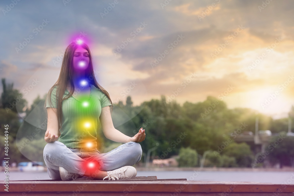 Teenage girl meditating near river. Scheme of seven chakras ...