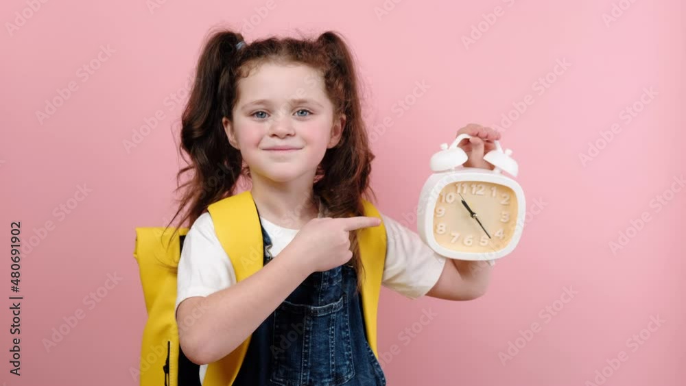Portrait of positive cute schoolgirl kid pointing finger on big clock ...