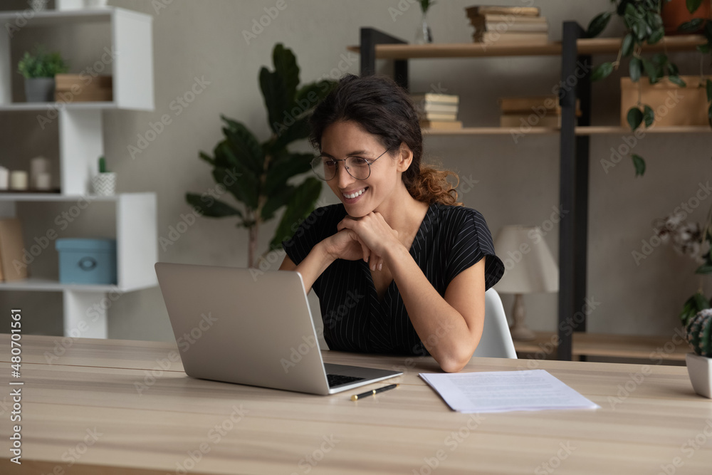 Smiling attractive millennial woman in glasses looking at computer ...