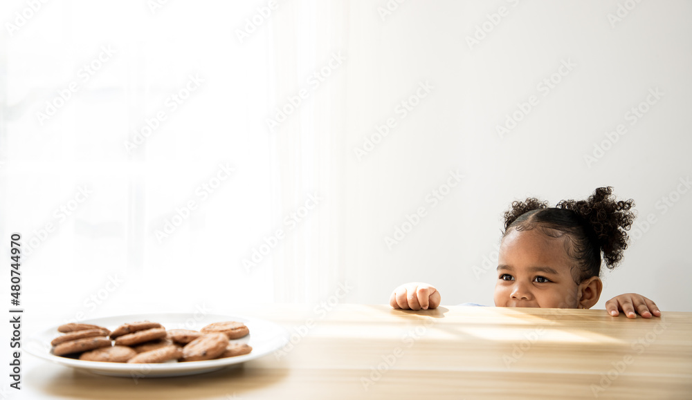Girl taking a cookie biscuit in the kitchen while her parents are ...