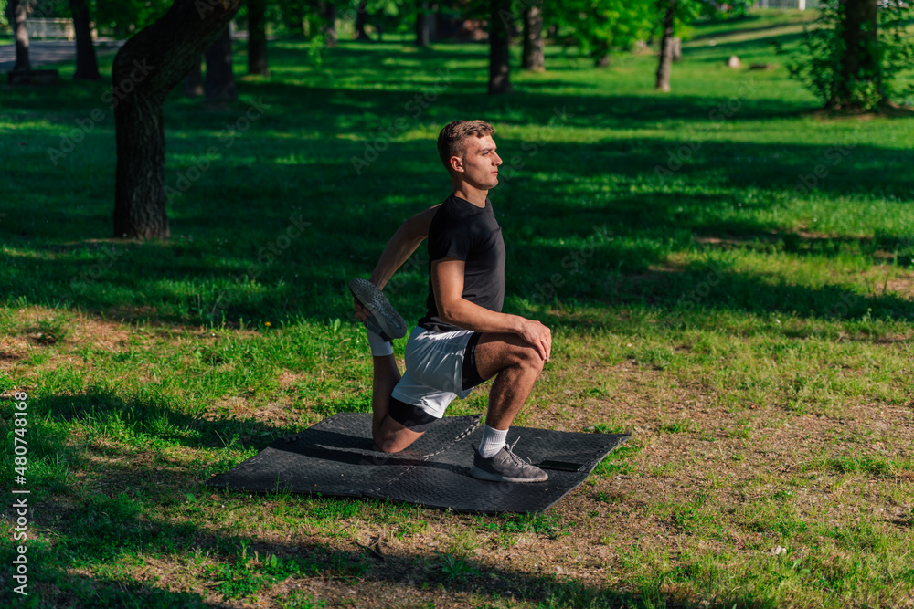 Sporty young man stretching legs and doing forward lunge while having ...