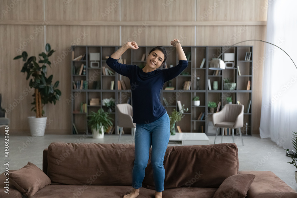 Happy energetic young Indian woman jumping barefoot on cozy sofa ... Happy energetic young Indian woman jumping barefoot on cozy sofa ...