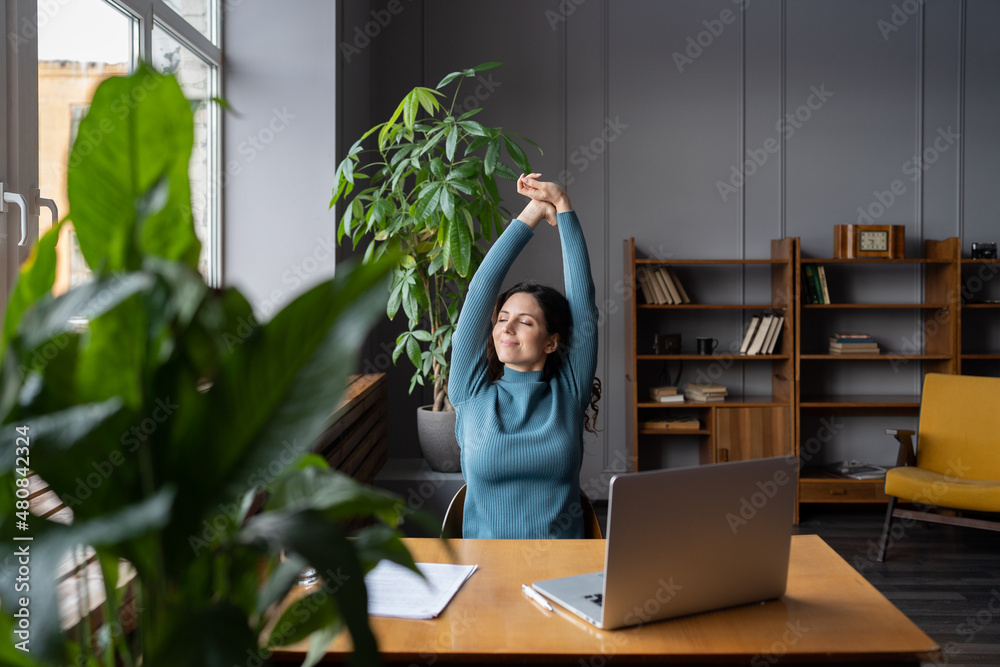 Relaxed office worker woman stretching hands and body taking break from ...