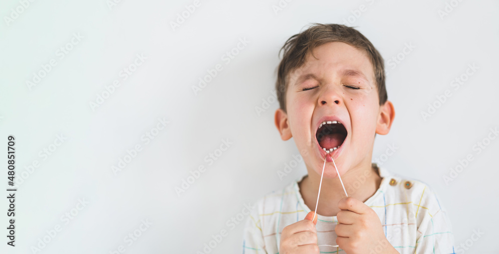 Cute boy pulling loose tooth using a dental floss. The boy's first milk ...